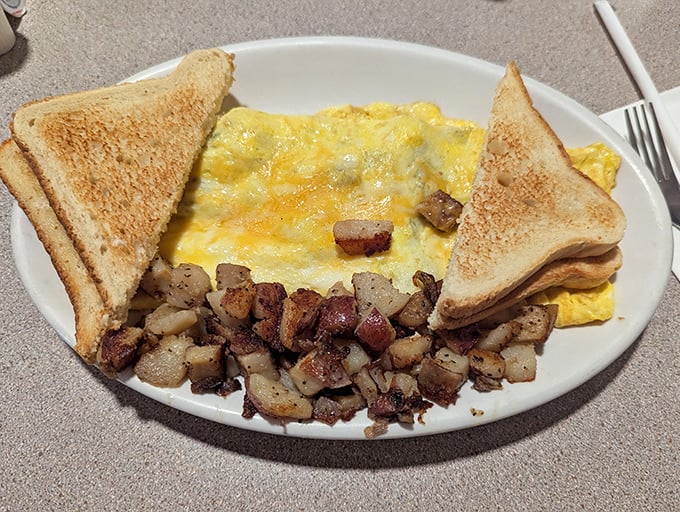 Behold the perfect omelet—golden, fluffy, and generous—flanked by home fries that could make a potato farmer weep with pride and toast that actually tastes like bread.