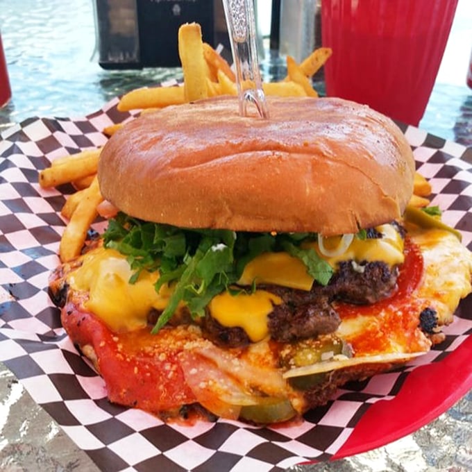 Behold the burger in its natural habitat: juicy, cheese-draped, and nestled on a checkered paper throne. That knife isn't decoration—it's structural support. 