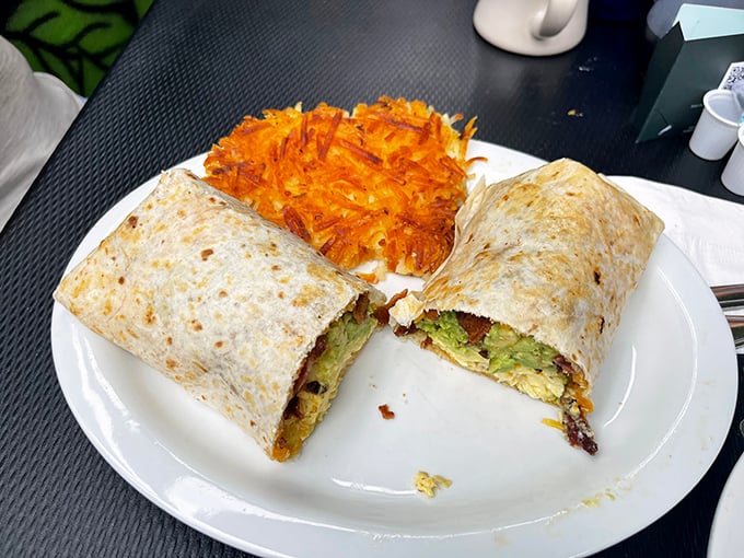 Behold the breakfast burrito in its natural habitat—golden-brown, stuffed with avocado and eggs, with a side of hash browns that could make a potato weep with pride.