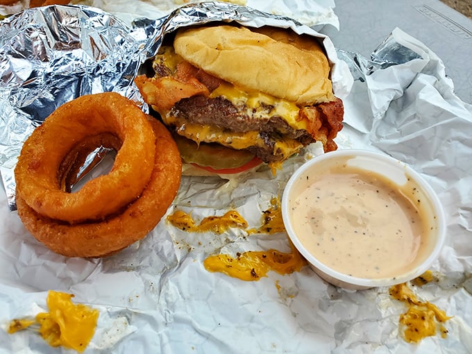 Behold the bacon cheeseburger in its natural habitat—wrapped in foil, accompanied by a golden onion ring, and destined for immediate consumption.