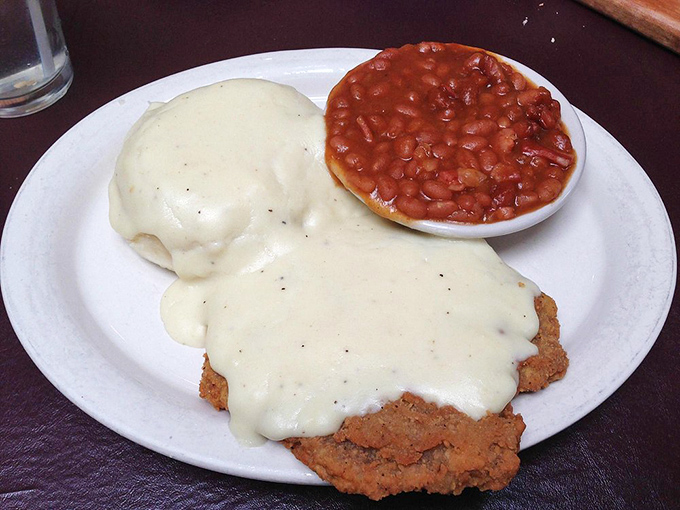 Behold the chicken fried steak in its natural habitat—swimming in creamy gravy with baked beans standing by for moral support.