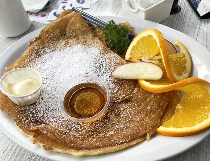 Behold the Danish pancake in all its glory: delicate, dusted with powdered sugar, and flanked by fresh fruit like edible artwork.