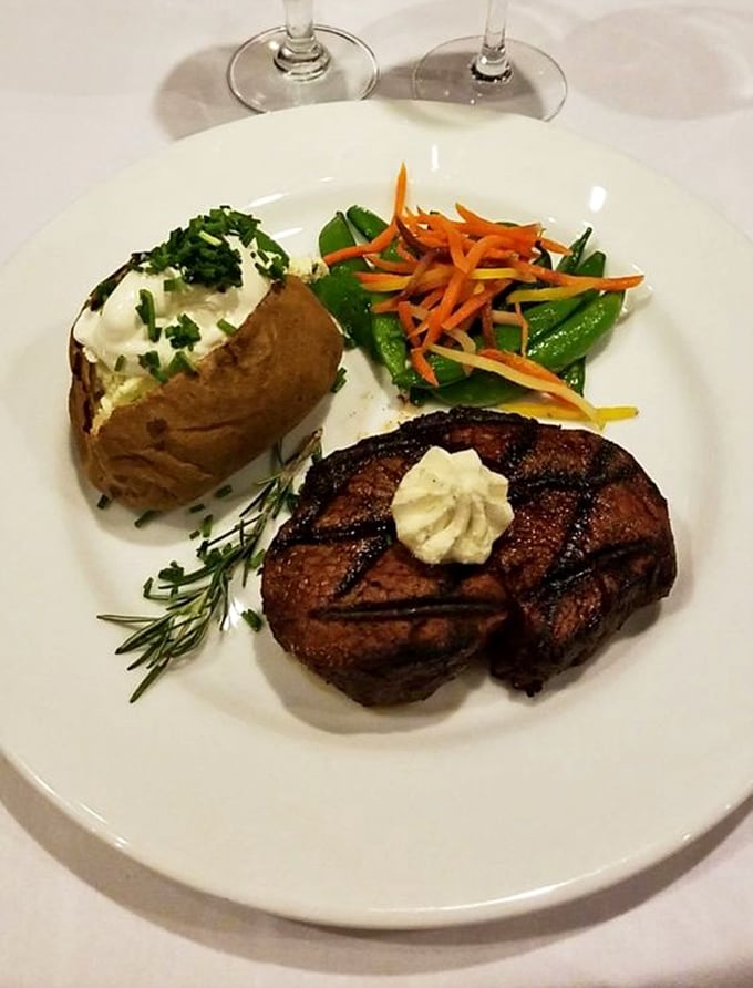 Behold the filet mignon in its natural habitat – perfectly seared, topped with herb butter, and flanked by a loaded baked potato that's practically begging to be devoured.