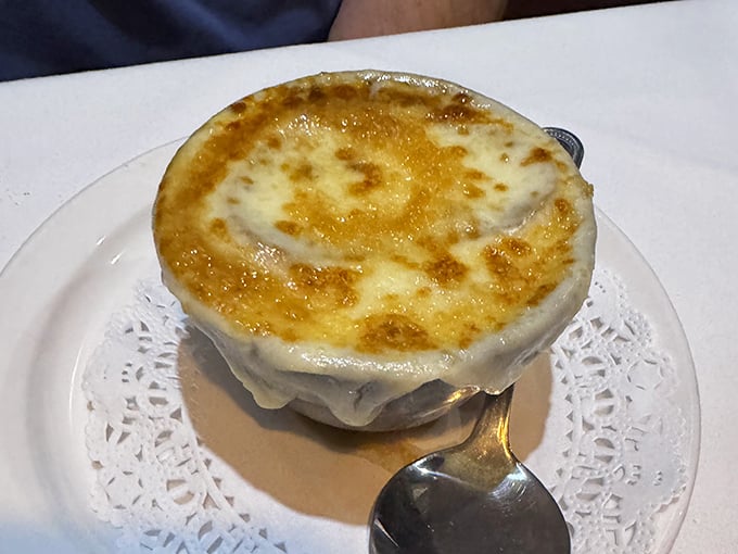 The French onion soup arrives like a work of art – that golden, bubbling cheese canopy hiding a treasure of caramelized onions and rich broth below.