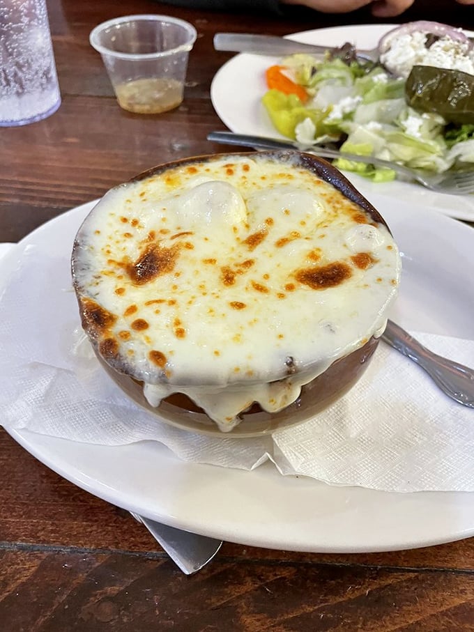 The French onion soup arrives like a cheese volcano mid-eruption—that golden, bubbling canopy protecting a savory treasure of caramelized onions below.