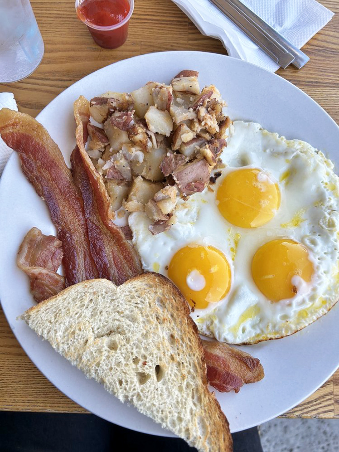 Breakfast perfection doesn't need filters—three sunny-side-up eggs, crispy bacon, and home fries that could make a potato proud.