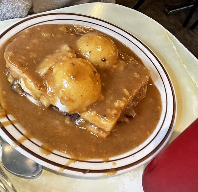 Hot beef sandwich nirvana—tender bread surrendering to a gravy flood while potatoes stand like delicious islands waiting to be discovered.