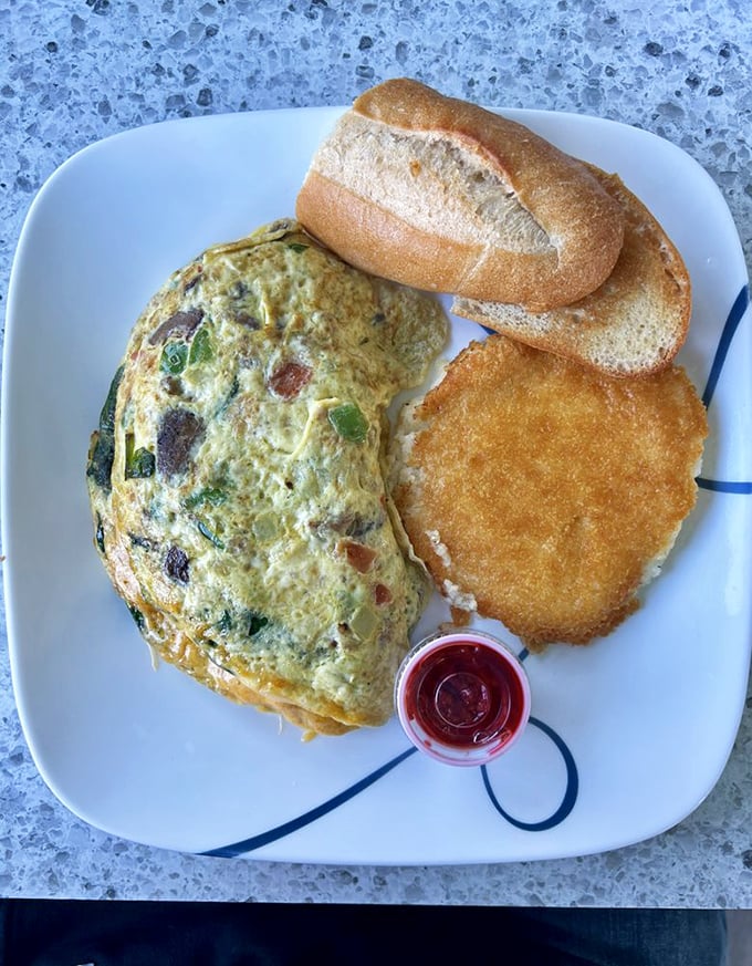 This isn't just an omelet; it's a masterclass in egg architecture—perfectly folded around vibrant veggies with a hash brown sidekick that deserves its own fan club.