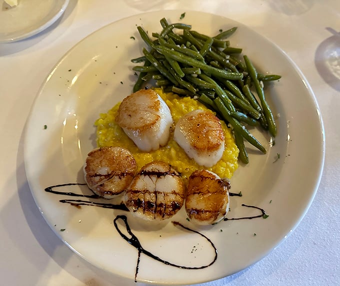 These scallops aren't just seared, they're transformed—golden-brown exteriors giving way to tender centers, perched atop saffron risotto like edible works of art.