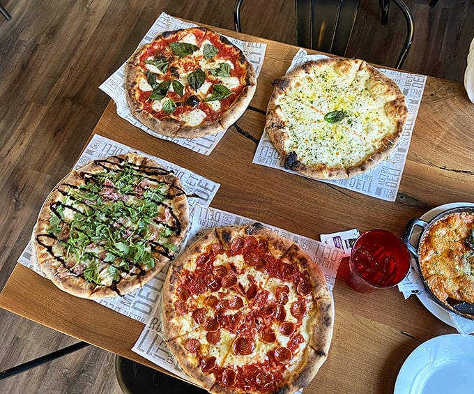 Pizza paradise on a wooden table. Four distinct pies that prove variety isn't just the spice of life—it's the whole meal.