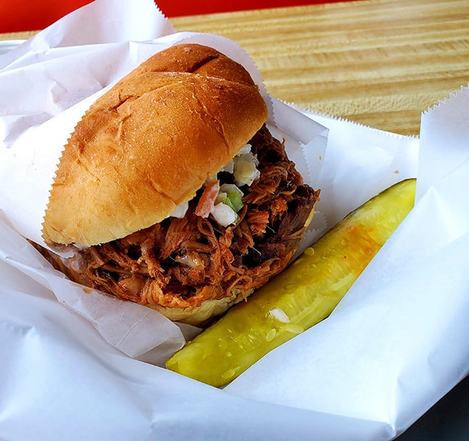 The pulled pork sandwich in all its glory—tender strands of smoky meat cradled in a soft bun with that pickle sidekick.