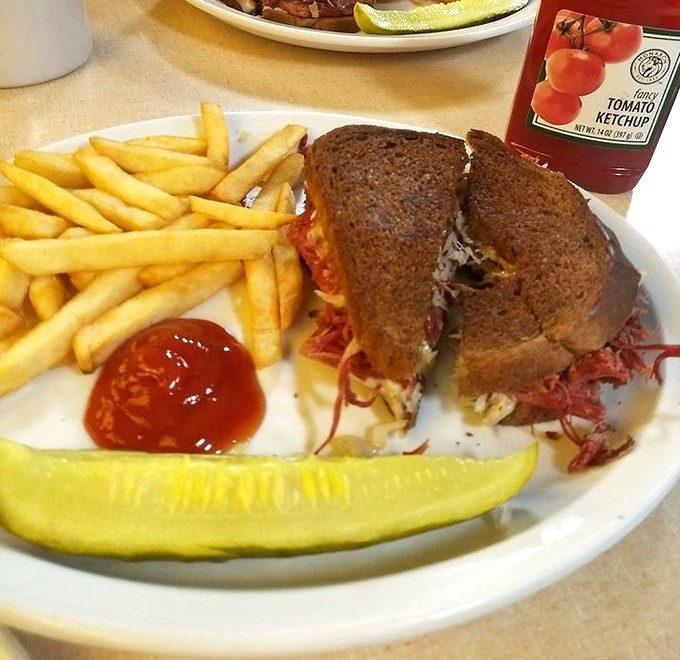 The legendary Reuben in its natural habitat—accompanied by crispy fries and a pickle spear. This isn't just a sandwich; it's architecture with sauerkraut.