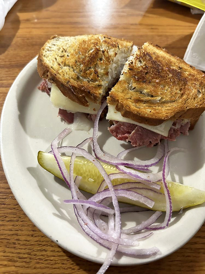 Behold the architectural marvel that is a proper Reuben—perfectly grilled rye, tender corned beef, and Swiss cheese with the obligatory pickle spear standing guard.