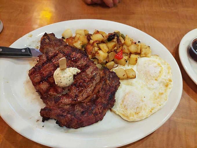 Behold the star of the show – a wood-smoked steak with perfect grill marks, accompanied by sunny-side-up eggs and home fries that could make a potato proud.