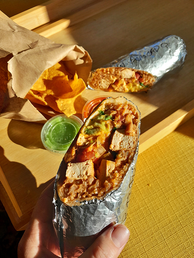 Behold the burrito in its natural habitat – foil-wrapped perfection alongside house-made chips and those little cups of salsa that somehow never contain enough.