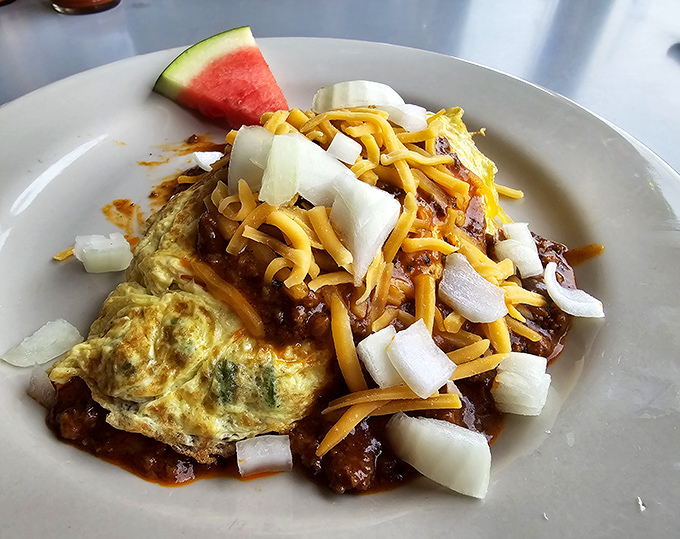 Behold the legendary Texas Omelet – a fluffy egg blanket wrapped around veggies, smothered in chili, and topped with enough cheese to make Wisconsin nervous.