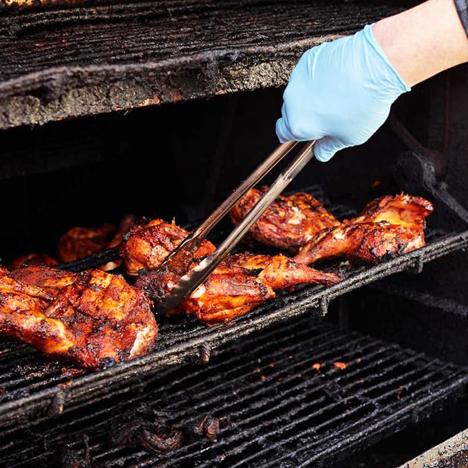 Tongs delicately lift chicken that's achieved barbecue nirvana – that perfect mahogany color that signals flavor has penetrated to the bone. Patience made visible.