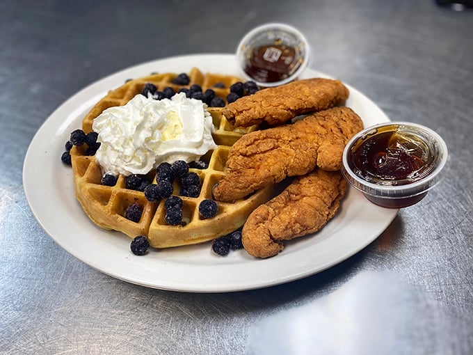 Golden waffles crowned with blueberries and whipped cream, flanked by crispy chicken tenders—breakfast and lunch having their most delicious argument on one plate.
