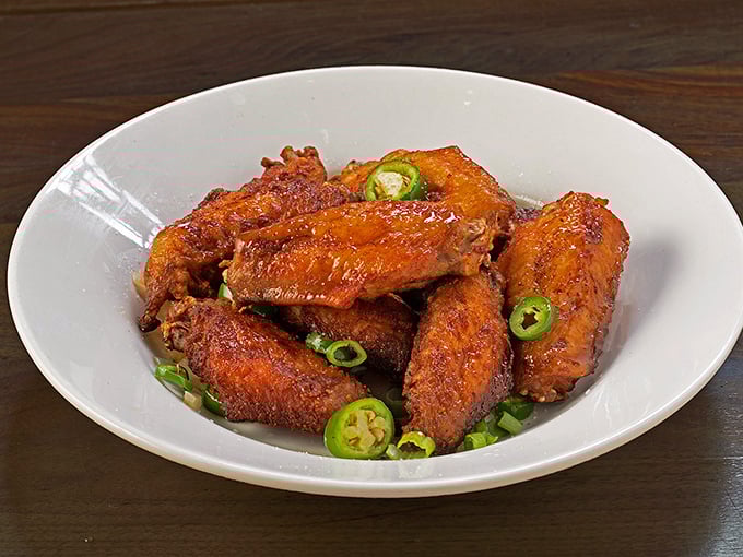 These aren't your average sports bar wings—they're crispy, glazed Malaysian-style flavor bombs topped with fresh jalapeños that will make Buffalo weep with jealousy.