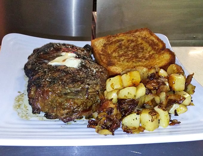 A perfectly seared ribeye with a pat of melting butter, golden toast, and home fries—proof that heaven exists on a white plate.