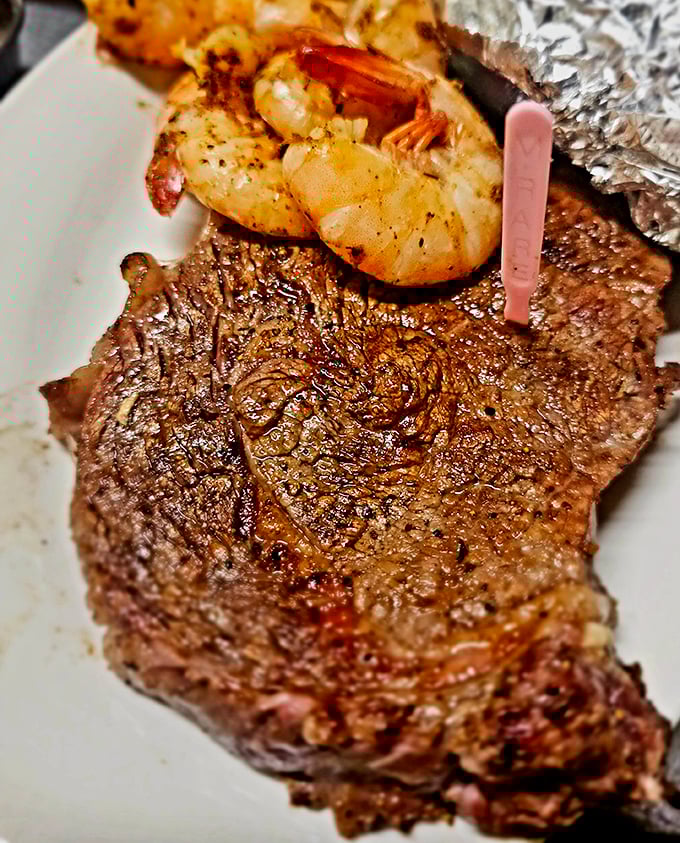 A perfectly seared ribeye with jumbo shrimp perched atop like a proud seafaring conquistador claiming new territory—surf and turf perfection.