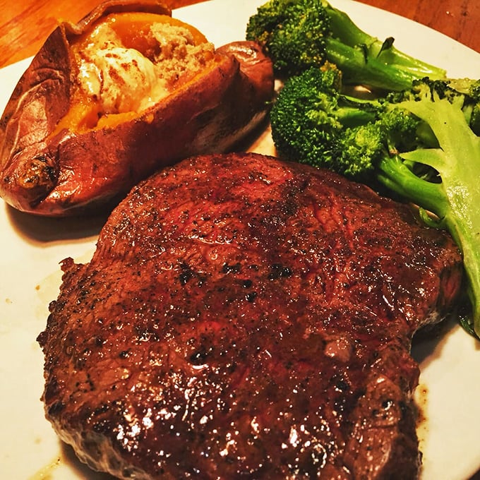 A perfectly seared steak shares the plate with a loaded baked potato and vibrant broccoli—the holy trinity of steakhouse satisfaction.