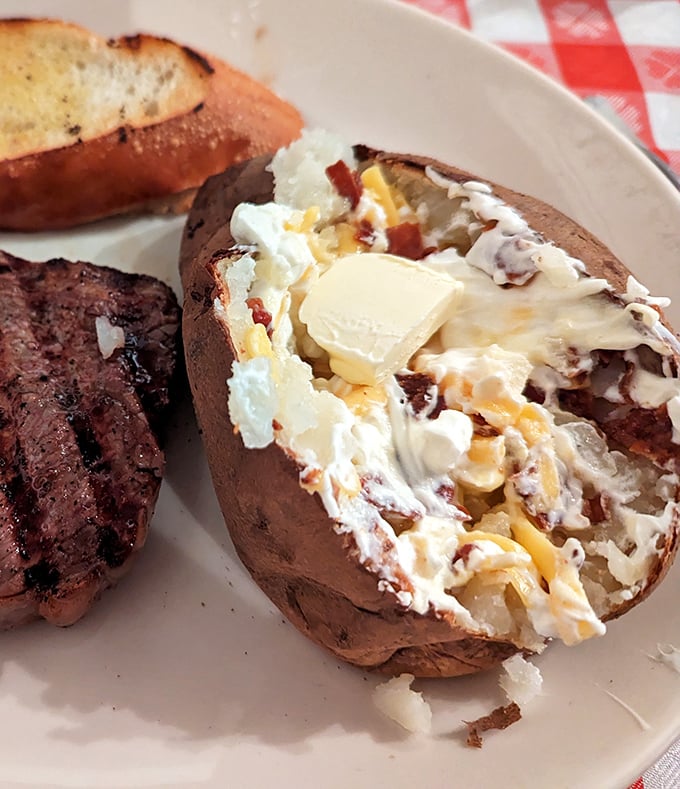 The loaded baked potato isn't a side dish—it's a co-star that deserves its own billing, complete with butter melting like a sunset.