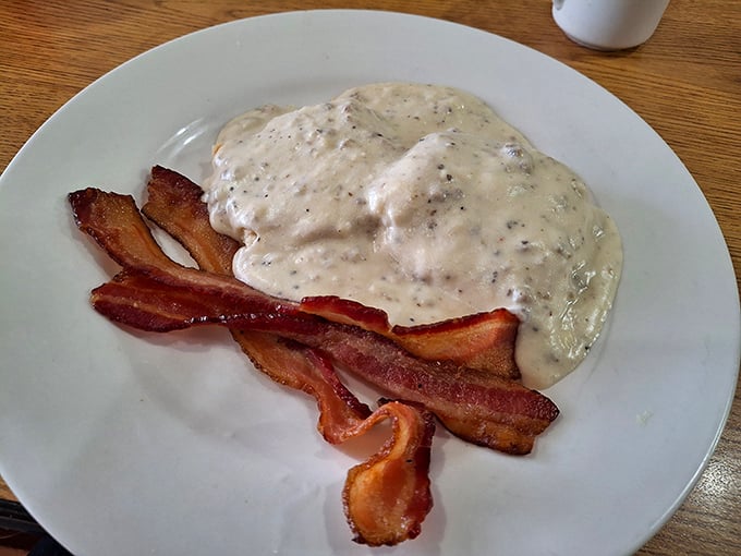 This isn't just biscuits and gravy – it's a warm blanket of peppery comfort atop fluffy biscuit clouds, with bacon standing by for moral support.