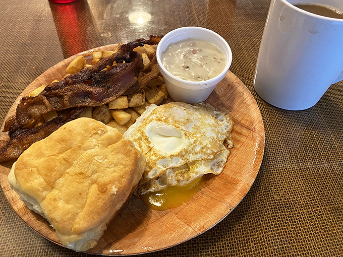 Breakfast perfection on a wooden plate: a sunny-side-up egg, golden biscuit, and crispy bacon—the holy trinity of morning happiness.