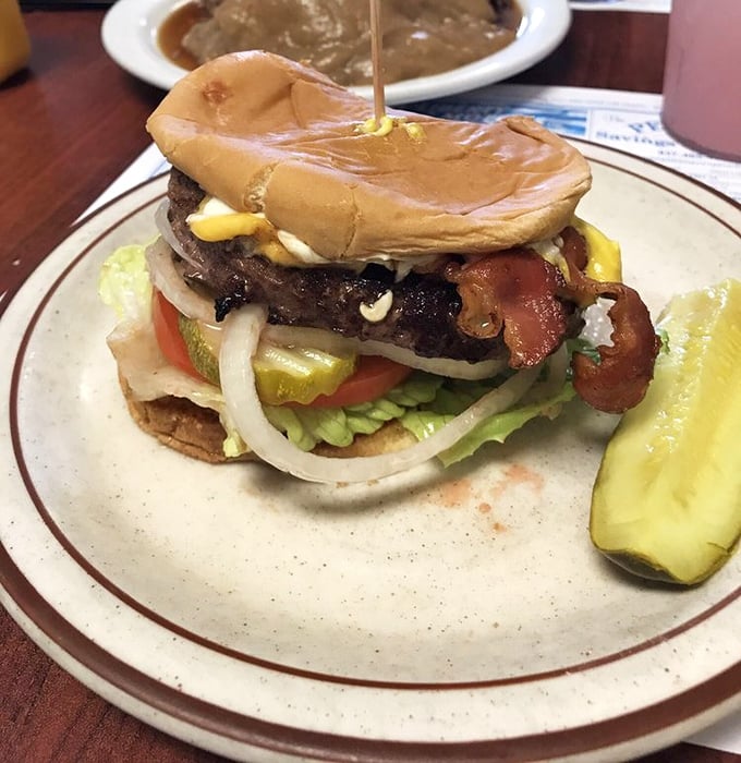 A burger that requires both hands and your full attention. That pickle spear isn't just garnish—it's the perfect palate cleanser between bites.