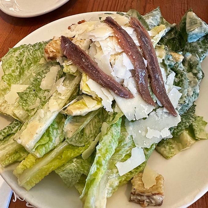 The Caesar salad arrives like Roman nobility—whole leaf romaine adorned with anchovy fillets and shaved Parmesan, no plebeian chopped salad here.