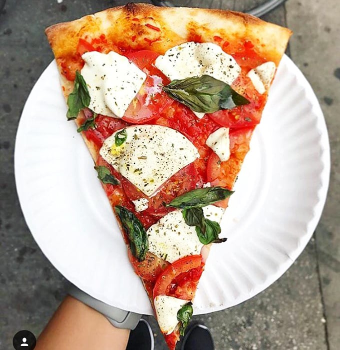 The Margherita slice—fresh mozzarella, vibrant tomatoes, and basil on a paper plate. Simplicity that makes you question why anyone would complicate pizza.