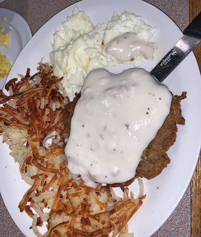 Chicken fried steak wearing a gravy overcoat with eggs and hash browns—the breakfast equivalent of winning the lottery on a Tuesday morning.