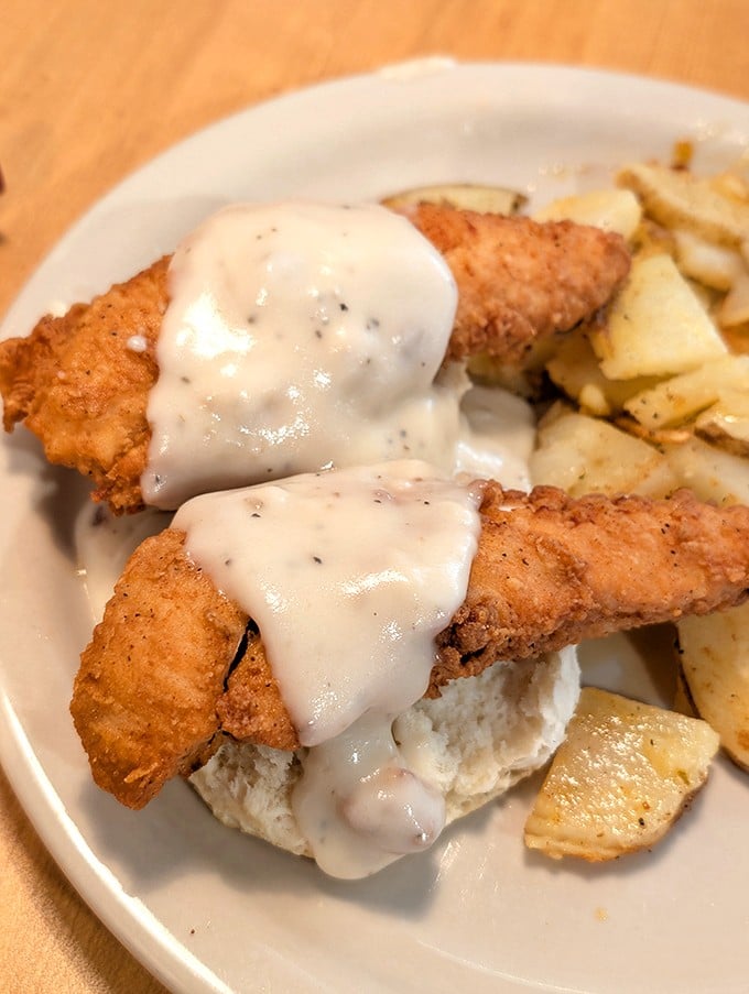 Comfort food perfection: golden-fried chicken tenders draped in country gravy atop a fluffy biscuit. Grandma would approve, then ask for the recipe.