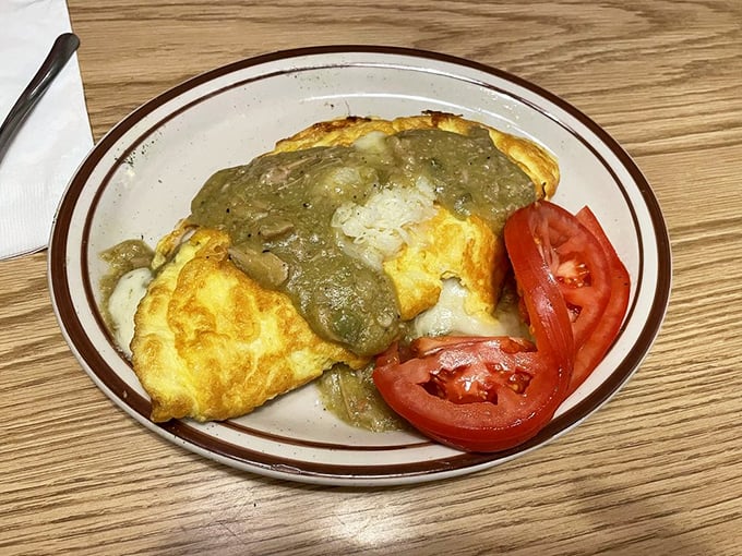 The Chile Verde Omelet arrives like a fluffy yellow pillow drenched in savory green goodness. Those homemade chips aren't just garnish, they're essential tools.