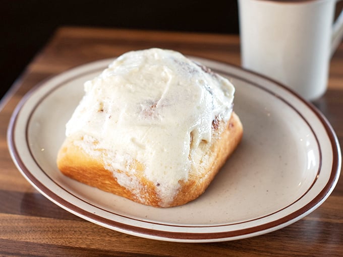 The cinnamon roll doesn't just arrive at your table—it makes an entrance, wearing its frosting like a decadent winter coat that's melting in all the right places.