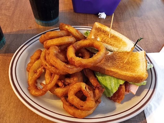 The onion rings form a golden fortress around a sandwich that's dressed better than most people at church on Sunday.