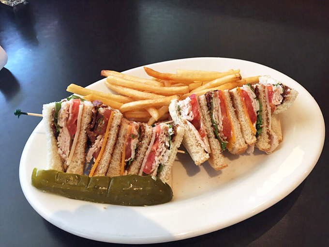 A club sandwich that's architectural perfection – layers of goodness standing tall like delicious skyscrapers with a pickle spire.