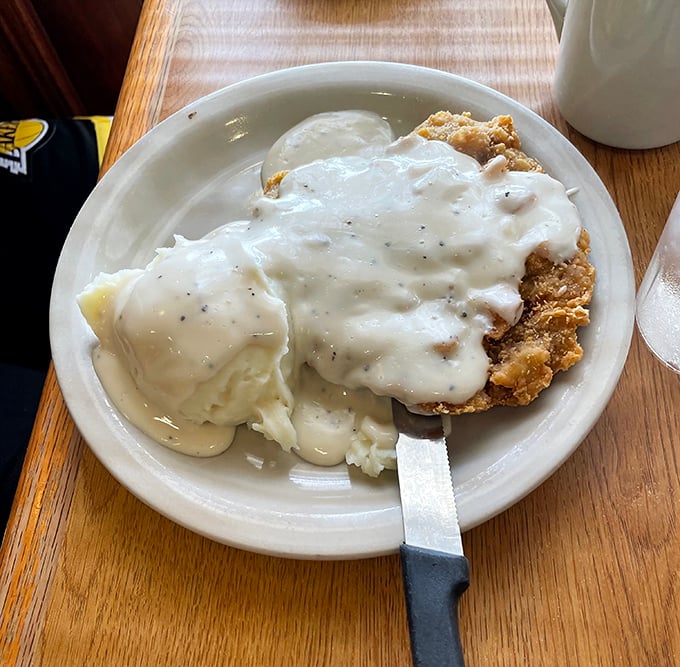Country fried steak swimming in creamy gravy alongside mashed potatoes – the kind of plate that makes diets wave white flags of delicious surrender.