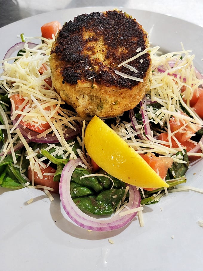 This isn't just any crab cake; it's a golden-crusted island of seafood perfection floating on a sea of fresh greens.