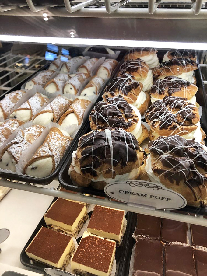 Cannoli on the left, chocolate-topped cream puffs on the right—this display case is essentially the United Nations of pastry diplomacy, bringing people together one sweet bite at a time.
