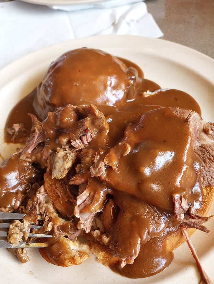 Hot beef sandwich that would make your grandmother nod in approval. This isn't food—it's a warm hug served on a white plate.