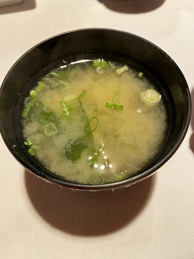 A bowl of miso soup that transcends its humble ingredients—delicate broth, dancing scallions, and the comforting warmth that signals the start of something wonderful.