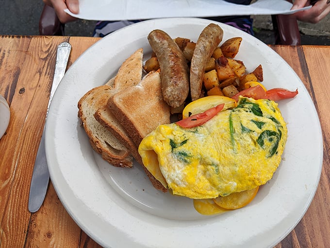 This omelet doesn't just sit on the plate—it commands attention with its perfect fold, vibrant fillings, and those home fries that deserve their own fan club.
