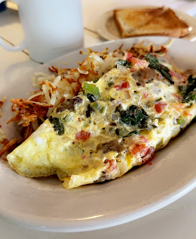 This isn't just an omelet—it's a masterpiece of morning architecture with perfectly folded eggs embracing a garden of fresh vegetables.