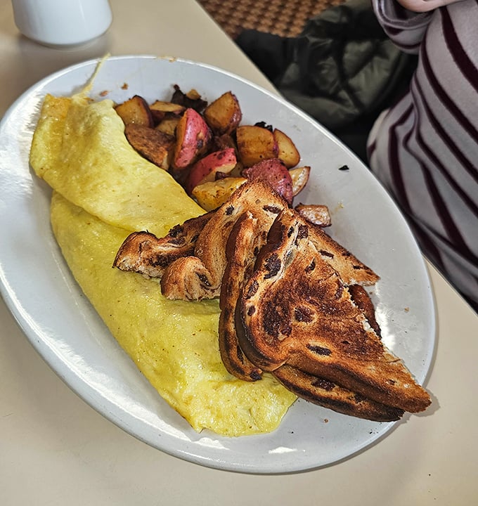 A perfectly executed omelet alongside marble rye and those legendary home fries – the holy trinity of diner breakfast excellence.