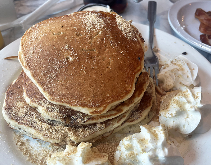 These pancakes aren't just stacked—they're practically skyscrapers of fluffy, golden goodness. The whipped cream melts into warm crevices like snow on a spring morning.