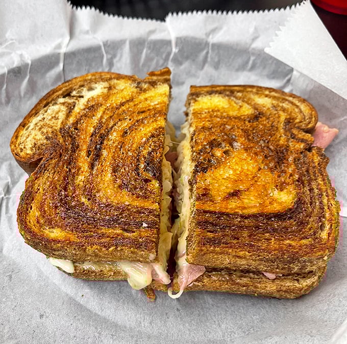 Behold the Reuben in its natural habitat—perfectly grilled bread revealing layers of corned beef, Swiss, and sauerkraut playing their delicious roles in perfect harmony.