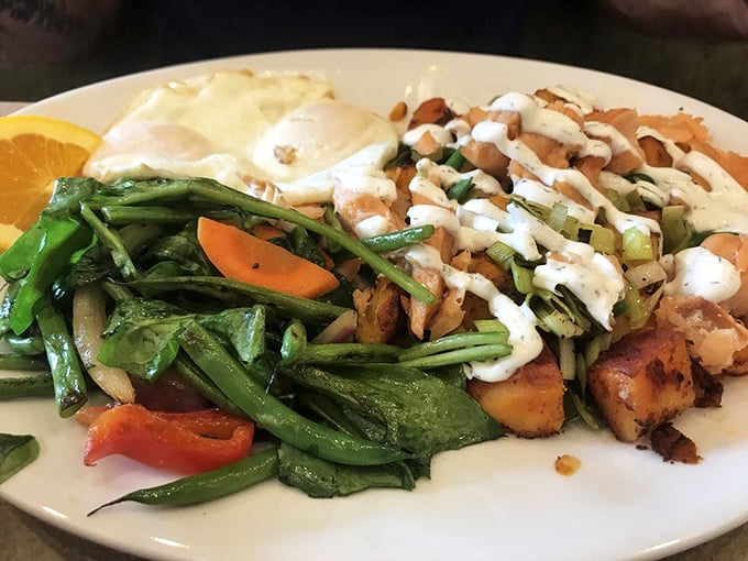 The Smoked Salmon Hash arrives like edible artwork—house-smoked salmon nestled among potatoes, vegetables, and poached eggs drizzled with lemon dill crème fraîche.