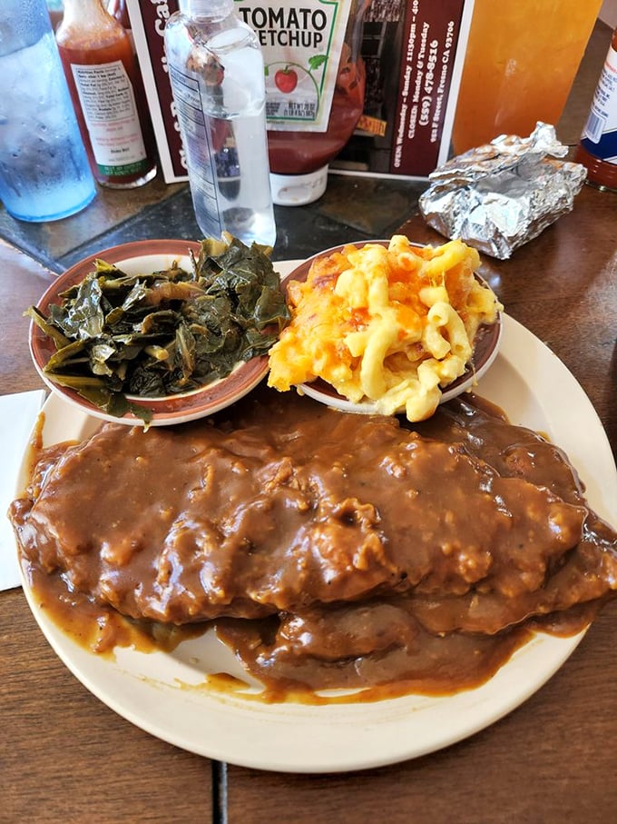 Smothered porkchop swimming in gravy alongside collard greens and mac & cheese—a holy trinity of comfort that makes Monday feel like Saturday.